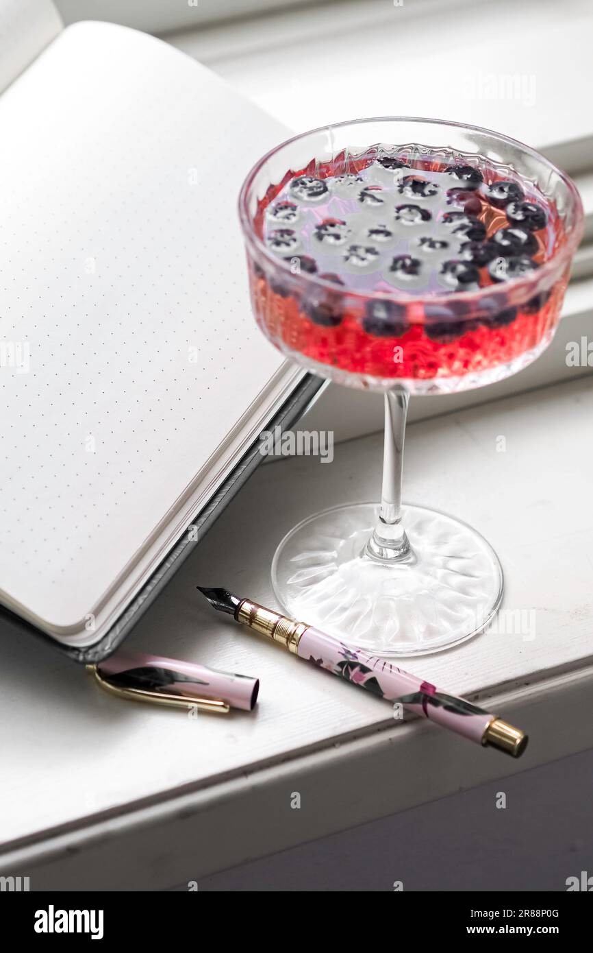 An open notebook with blank pages and a glass of red cocktail with ...