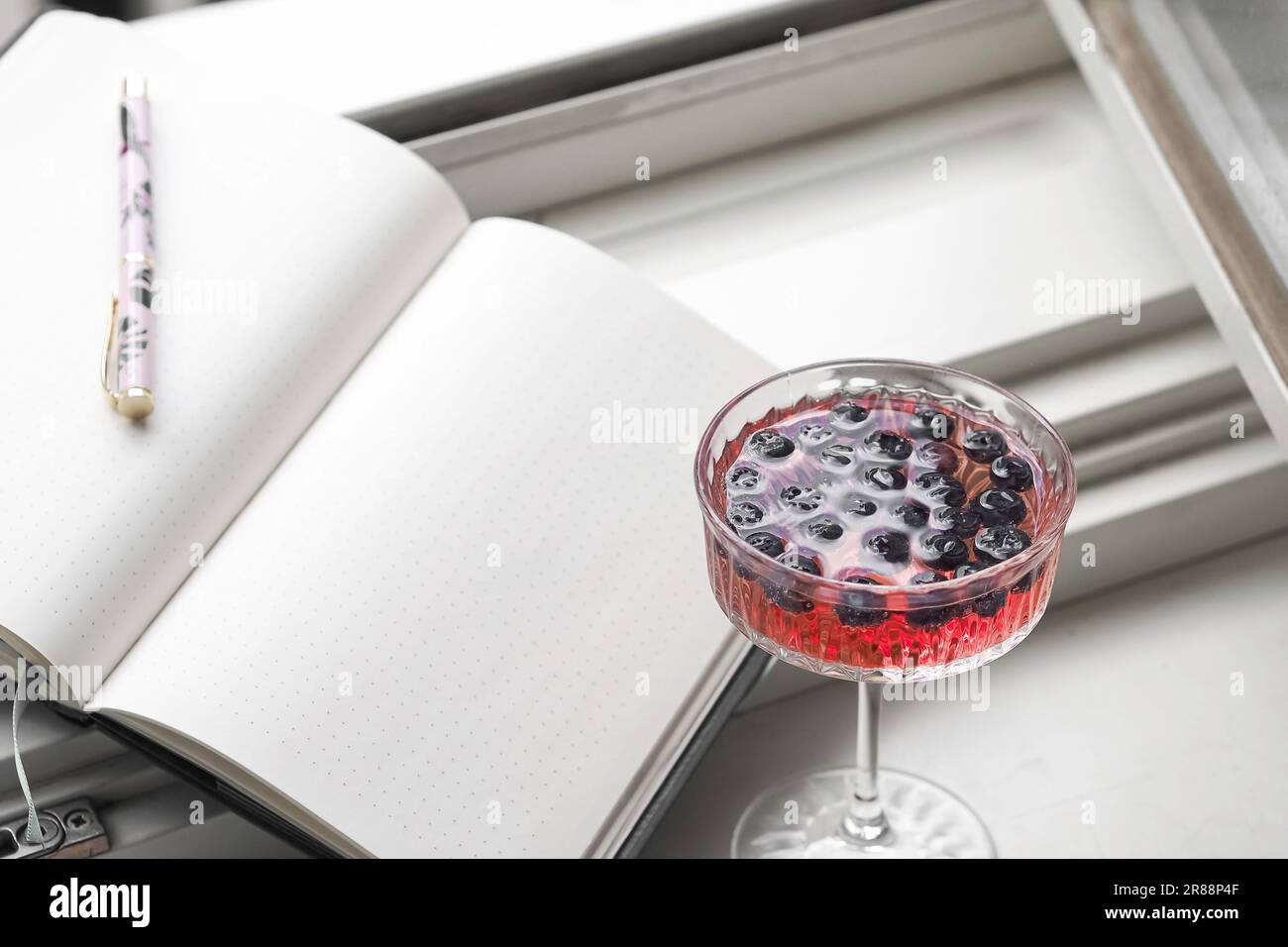 An open notebook with blank pages and a glass of red cocktail with ...