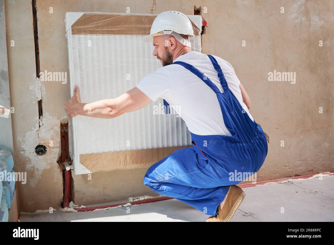 Male technician mounting heating radiator on the wall. Man wearing ...