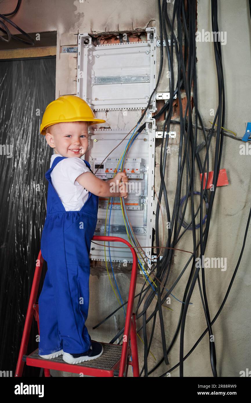 Smiling little boy in construction safety helmet holding electrical ...