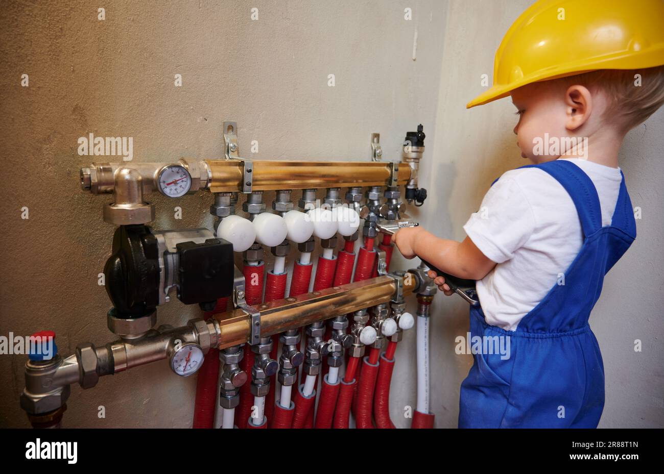 Baby boy in safety construction helmet using wrench tool while fixing ...