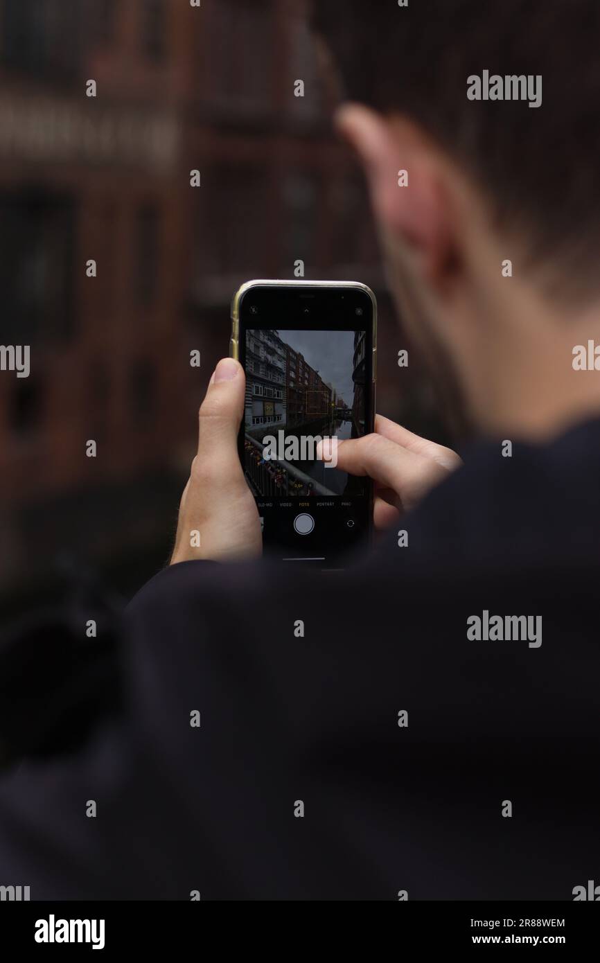 A man capturing a photo of a tall, modern building with his smartphone ...