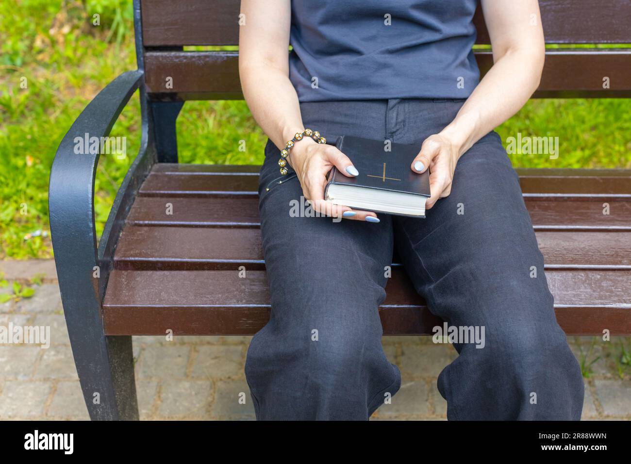a woman holding a bible in her hands sitting on a park bench. woman has ...