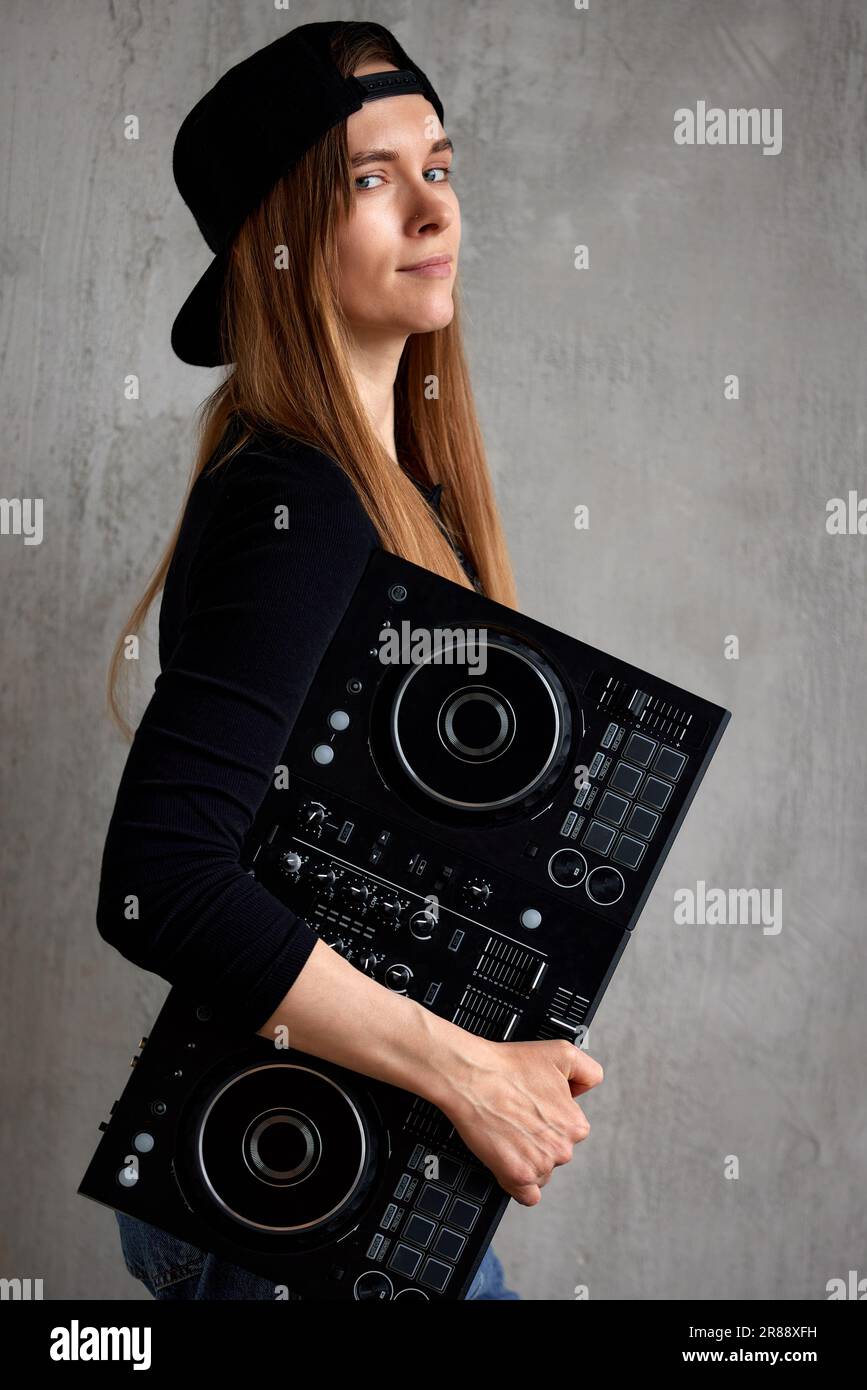 A young long-haired DJ girl in a black top, jeans and a black baseball ...