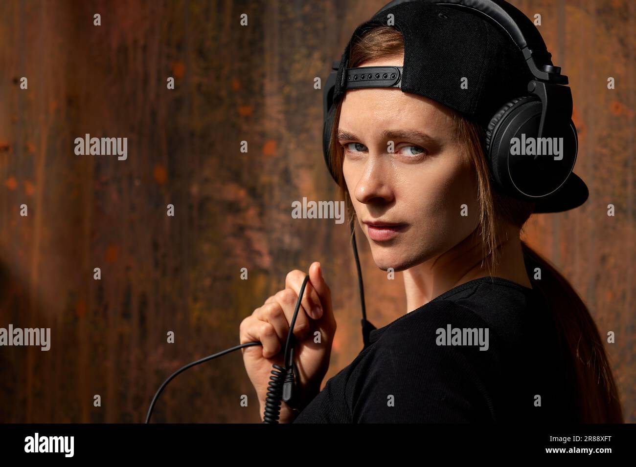 A young long-haired DJ girl in a black top, black baseball cap and ...