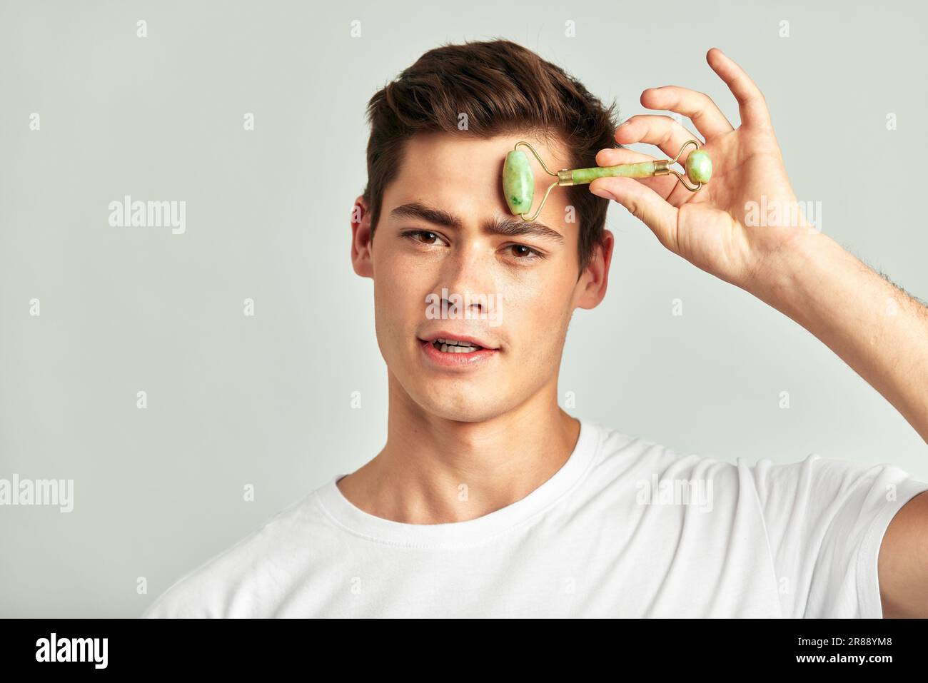 Young handsome smiling guy with brown hair in a white t-shirt using ...