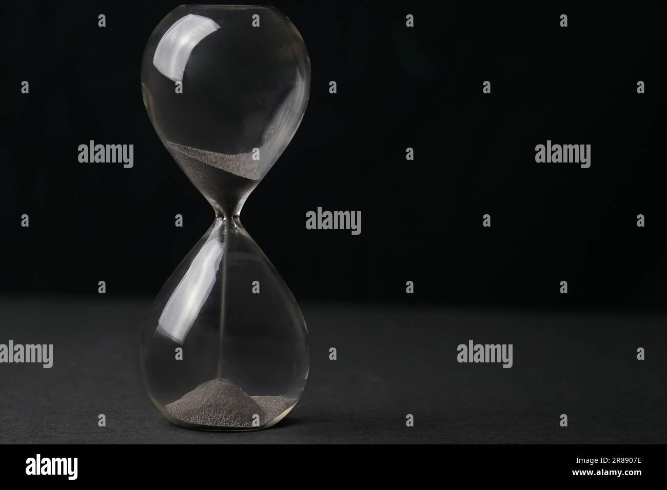 An hourglass with sand falling through, set against a black backdrop ...