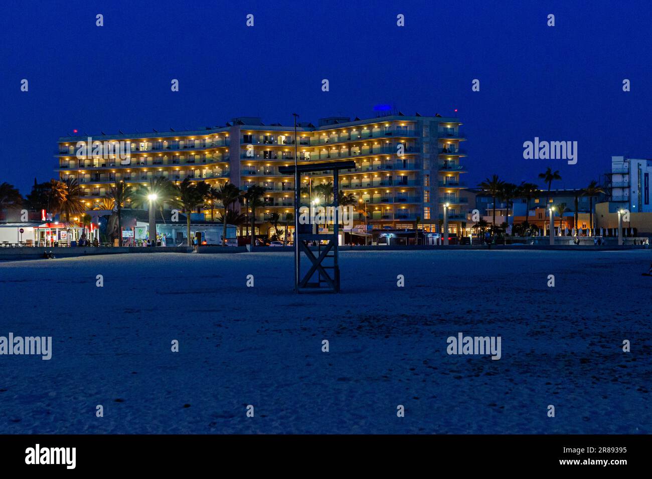 This image depicts a beachfront scene with multiple lit up buildings ...