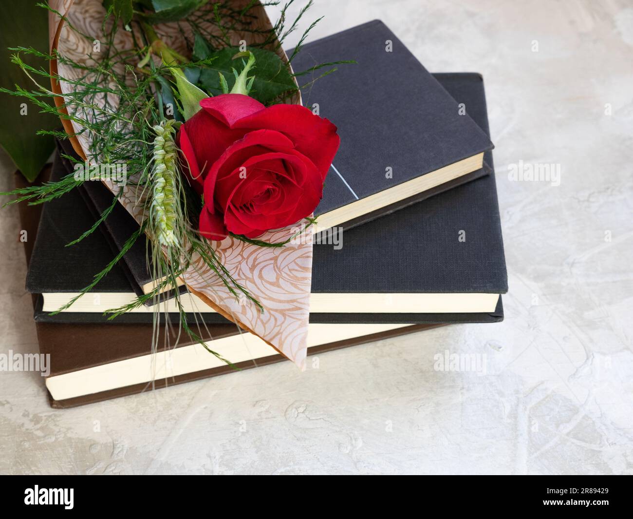 A radiant red rose bloom rests atop a stack of books on a white ...