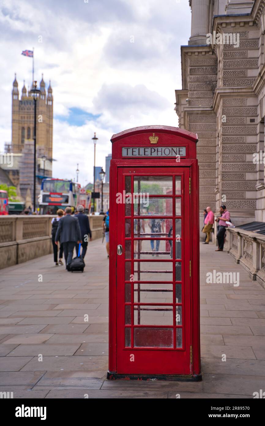 A traditional red telephone booth is situated on the sidewalk in front ...