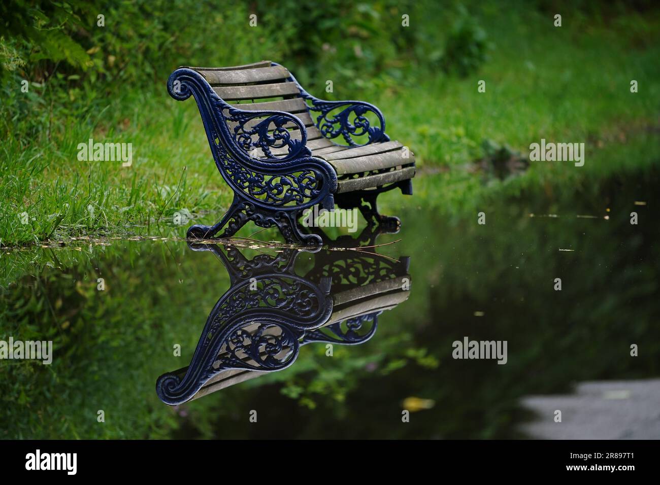 A bench is reflected in a puddle after rainfall in Sefton Park ...