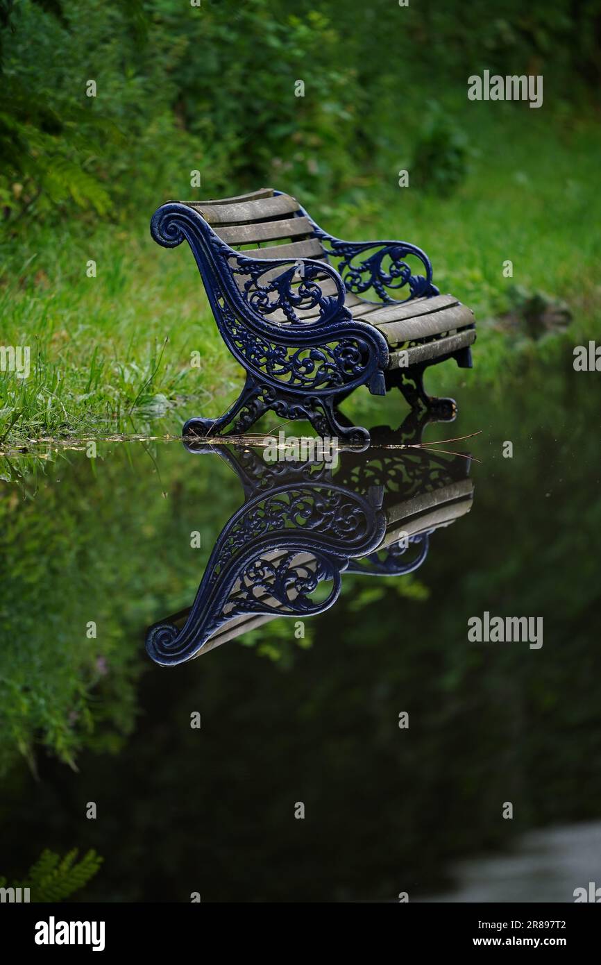 A bench is reflected in a puddle after rainfall in Sefton Park ...
