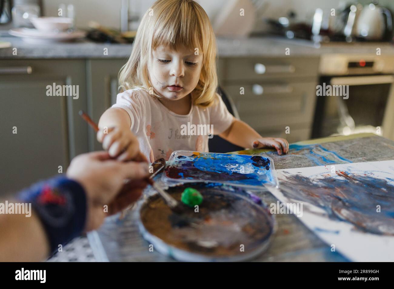 Father helping little girl painting with tempera paint using a ...