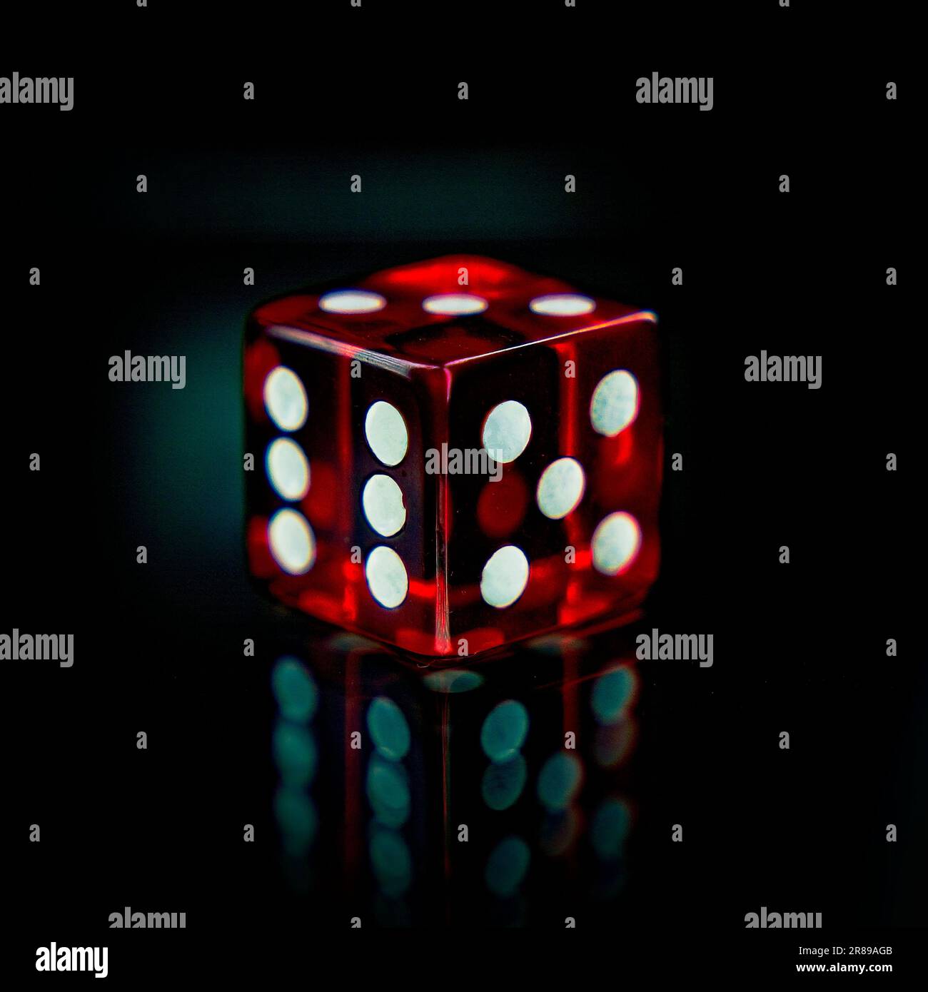 An isolated, transparent red dice cube resting atop a solid black ...