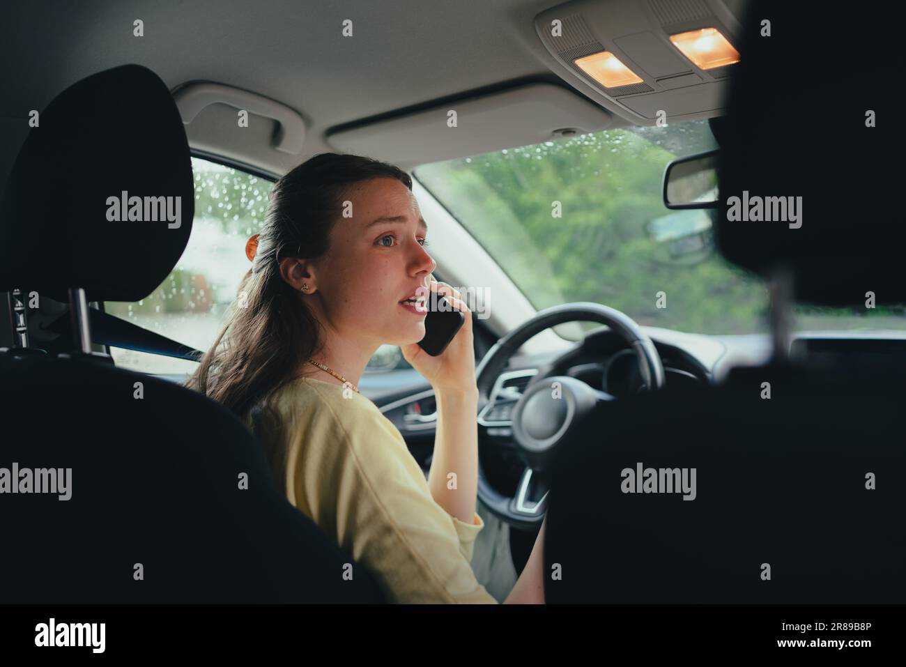 Scared young woman sitting in electric car with drained battery, making ...