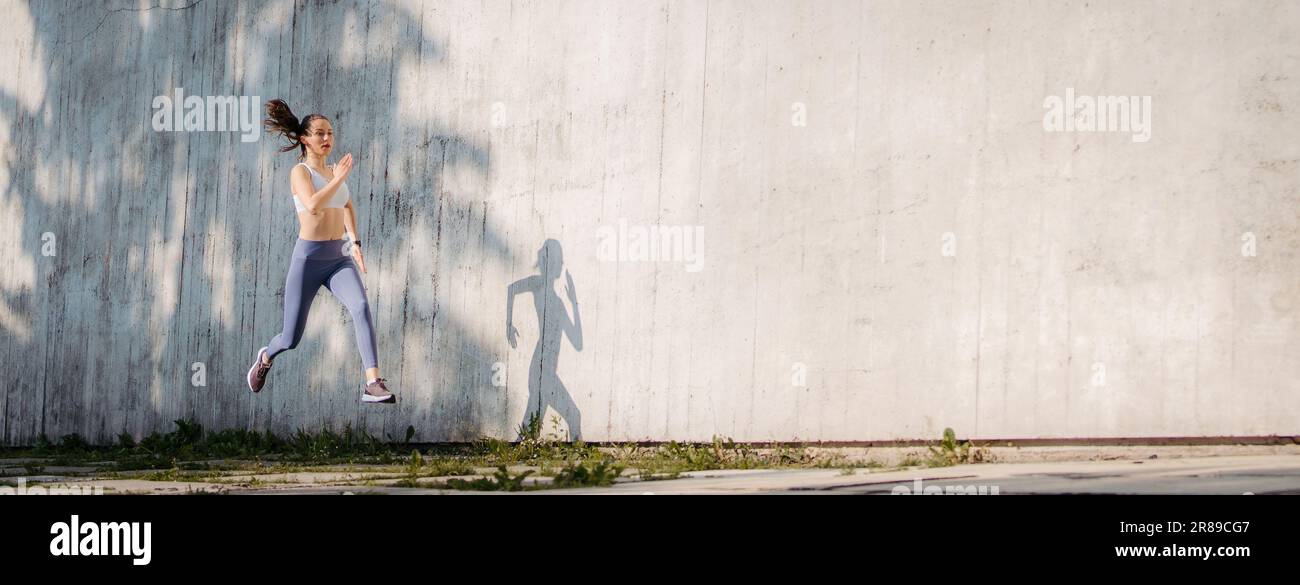 Fitness woman running in front of concrete wall casting shadow Stock ...