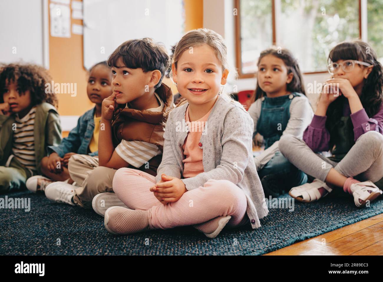 Adorable little child looking at the camera while sitting in class with ...
