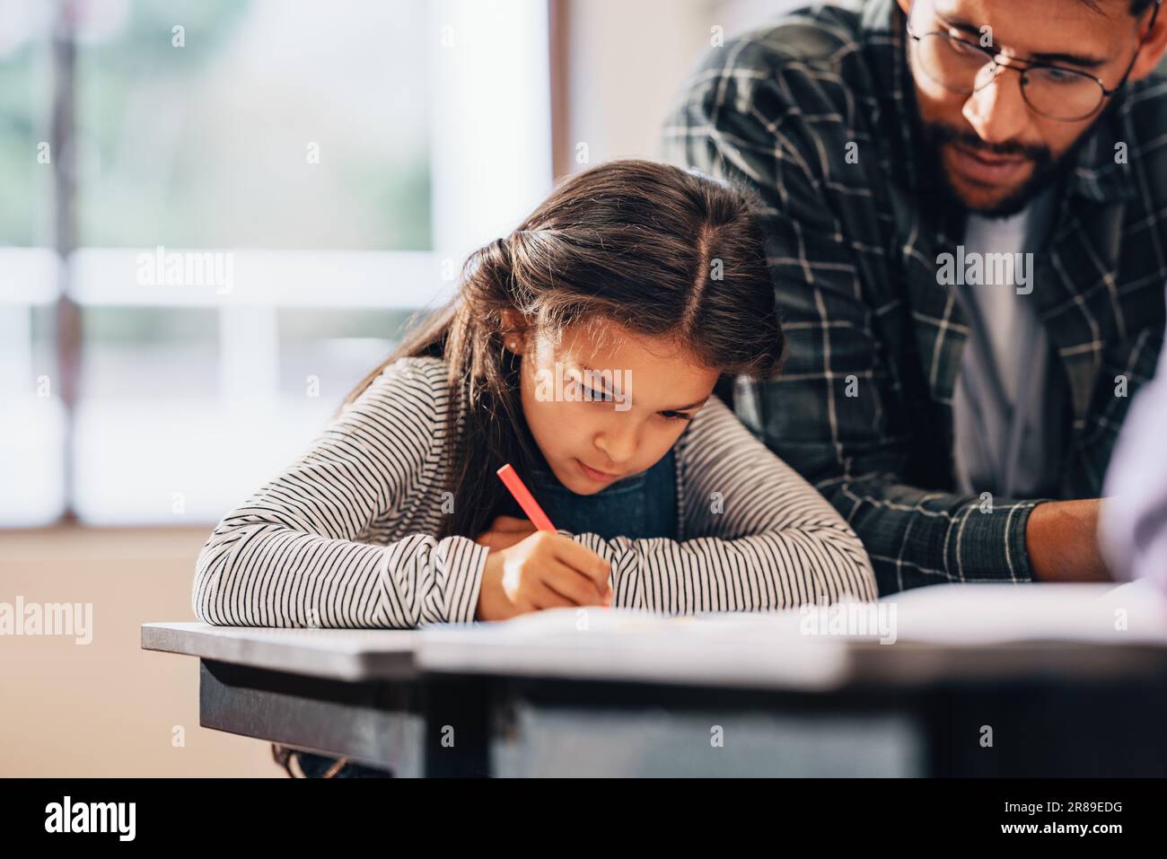 Young girl writing with a colouring pen with the help of her teacher ...