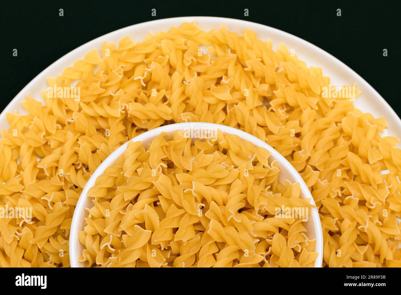 Uncooked Fusilli Pasta Lying on White Plate on Black Background. Raw ...