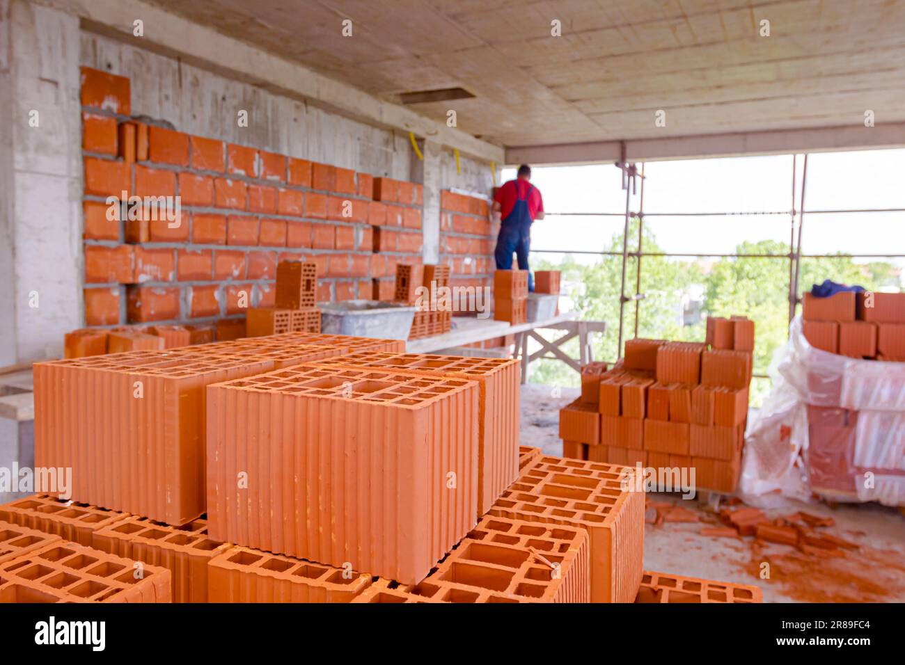 Heap of red ceramic blocks placed on wood platform on construction site. In background worker ...