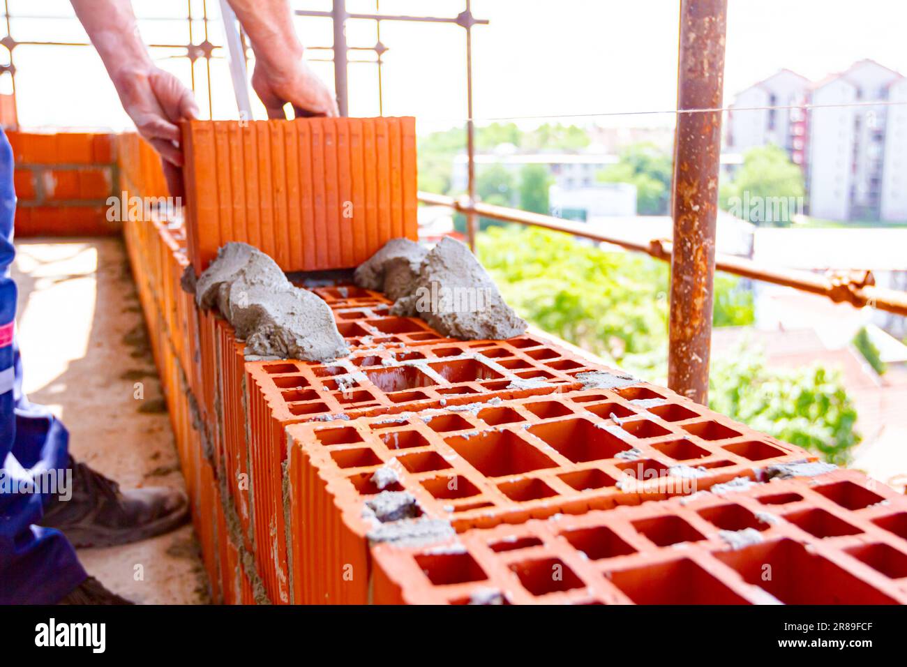 Mason, bricklayer worker is using red blocks to mount a wall next the ...