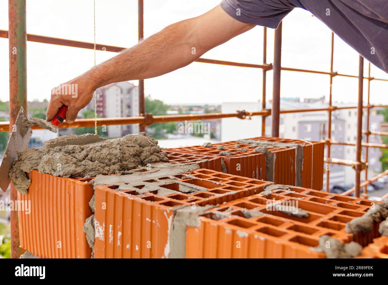 Worker is using spatula, trowel, to apply mortar on red blocks to make ...