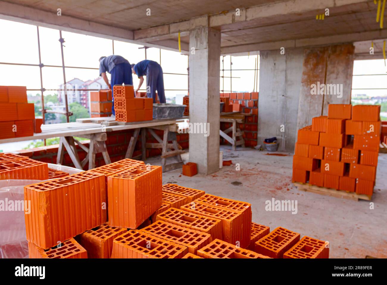 Heap of red blocks wait to be installed, in background masons are ...