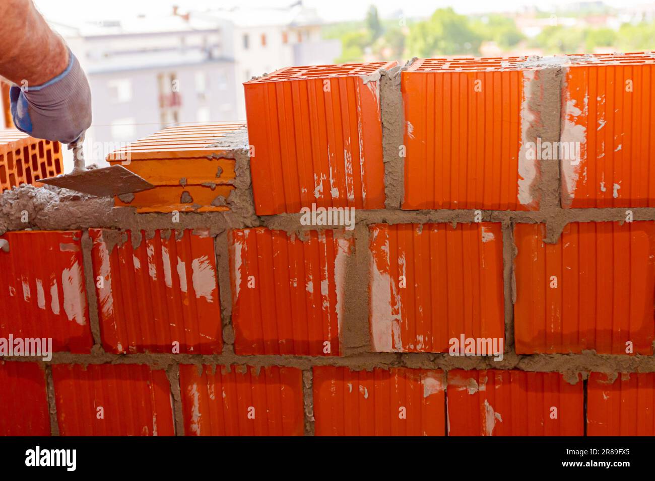 Worker is using spatula, trowel, to apply mortar on red blocks to make ...
