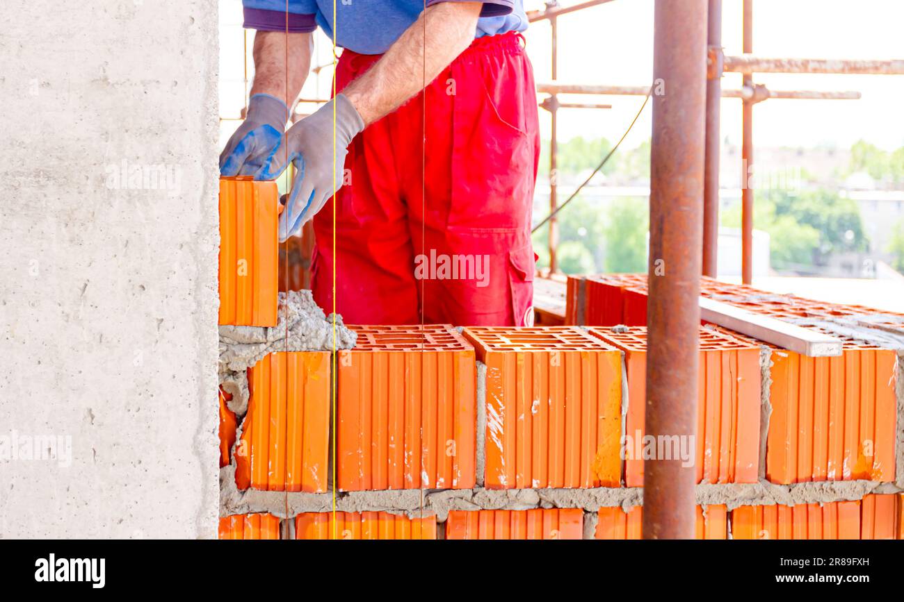 Mason, bricklayer worker is using red blocks to mount a wall next the ...