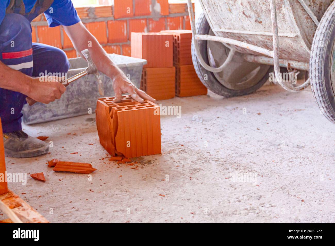 Worker breaks red ceramic block with mason's hammer, shortens it to ...