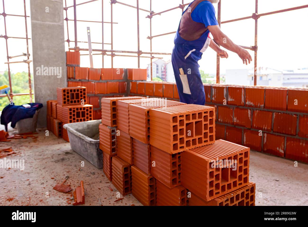 Heap of red blocks waiting to be installed, in background mason is ...