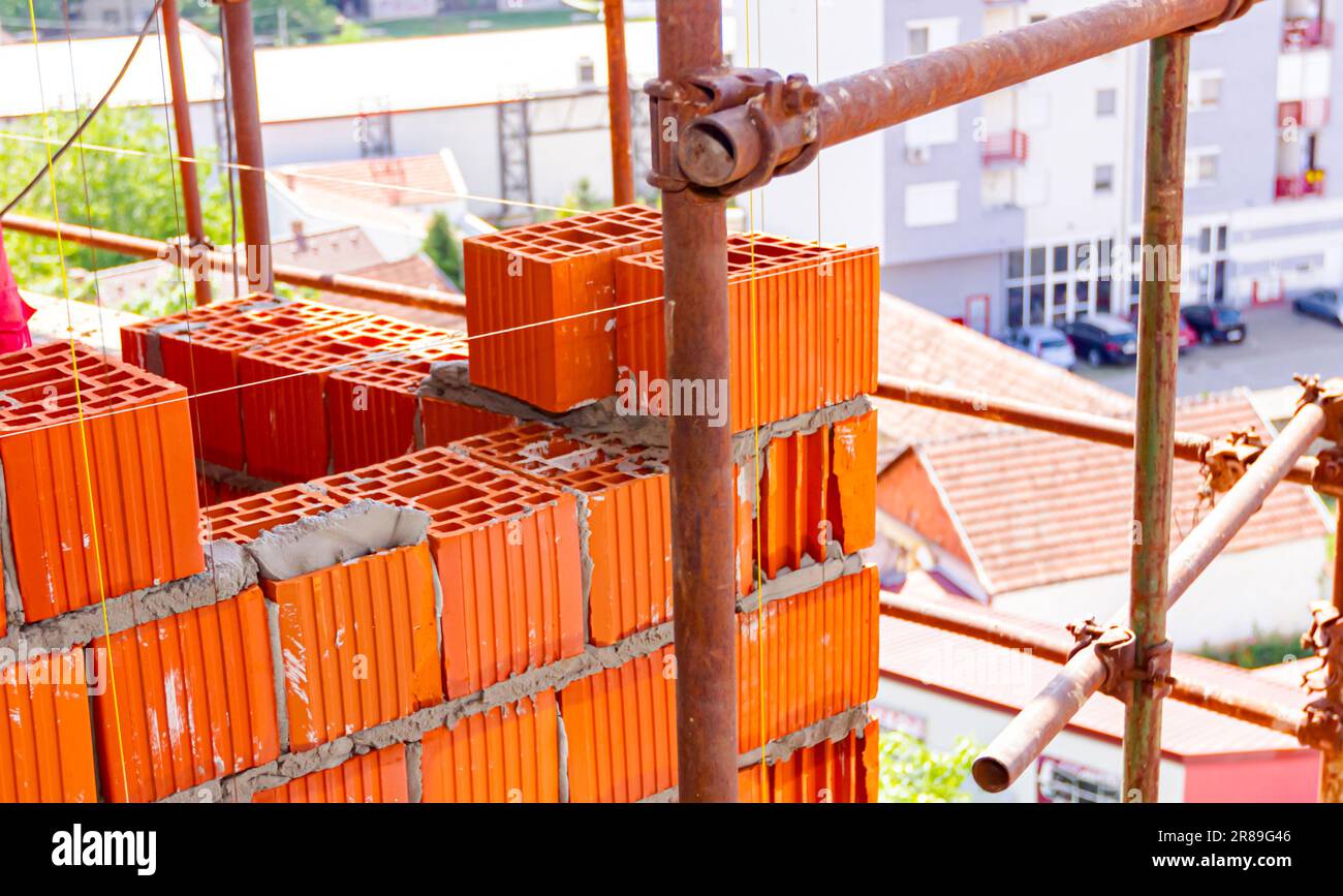 Wall edge with red blocks and mortar with rusty scaffold, building is ...