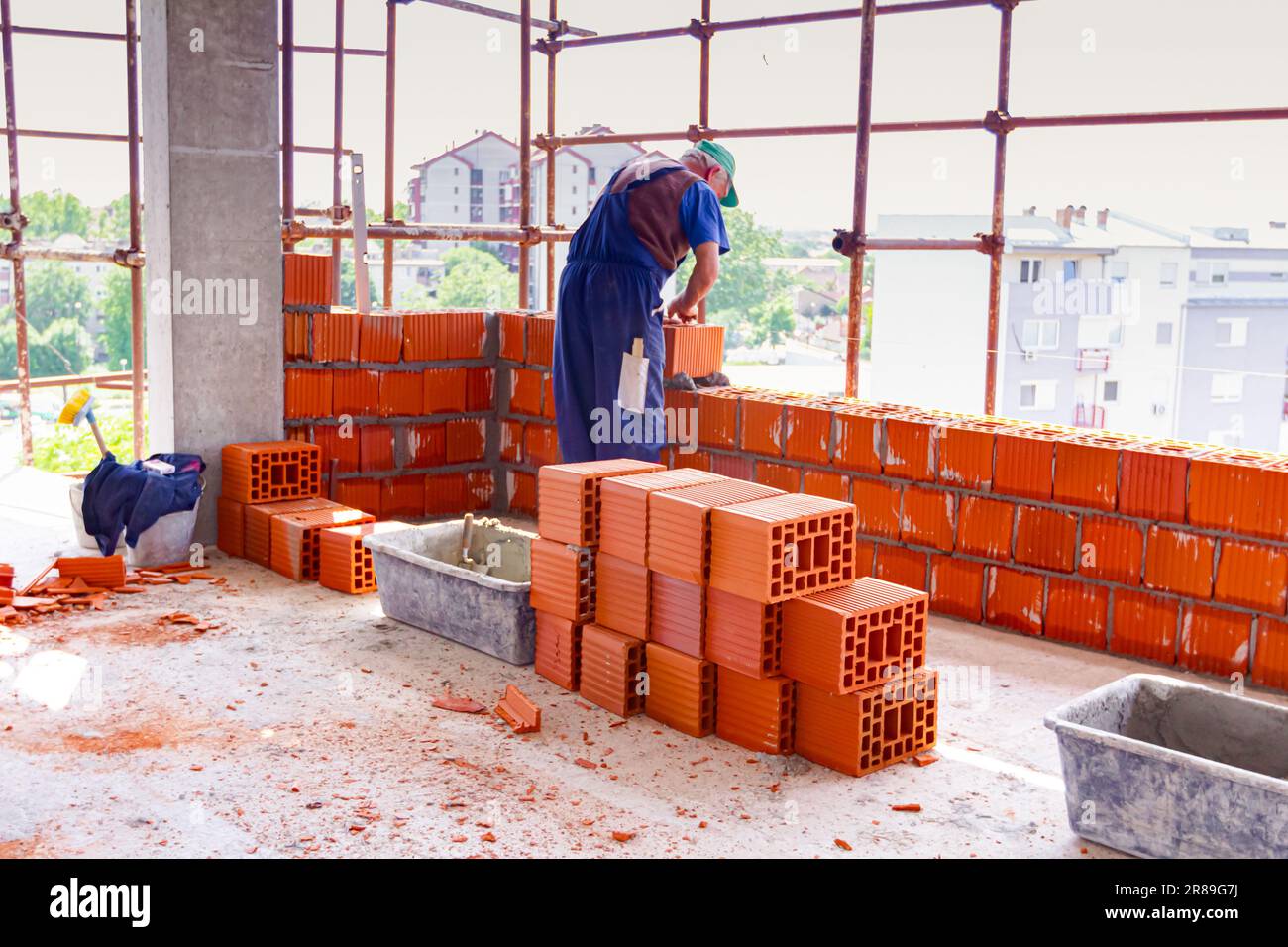 Heap of red blocks waiting to be installed, in background mason is ...