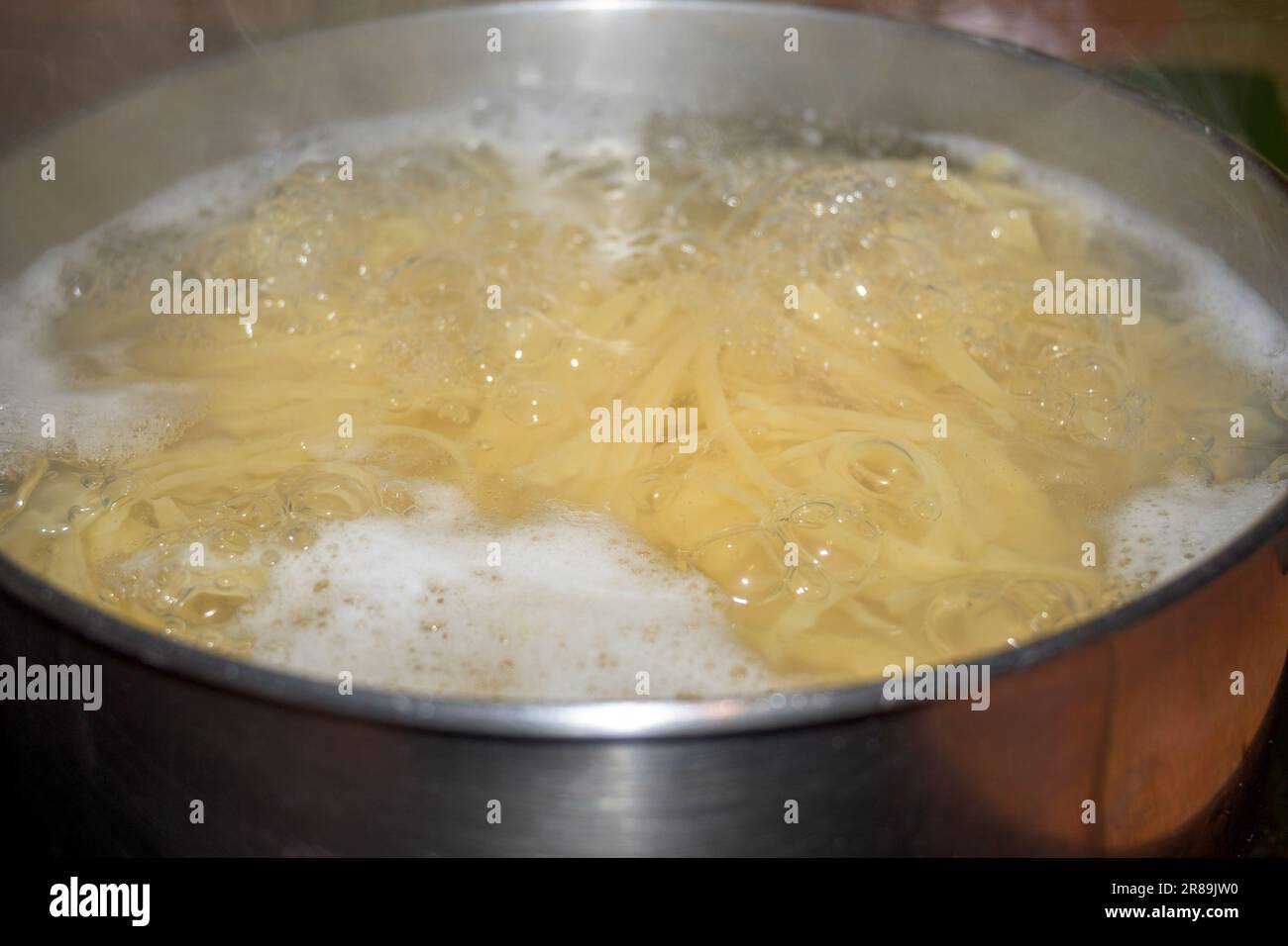 noodles cooking in a pot of boiling water with burning foam almost ...
