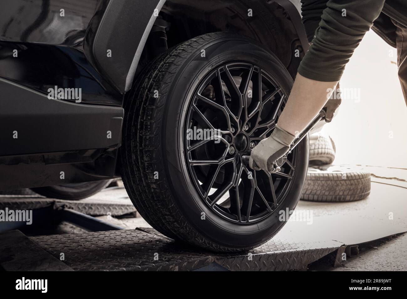 A master tire fitter screws a new black wheel to a car in a tire ...
