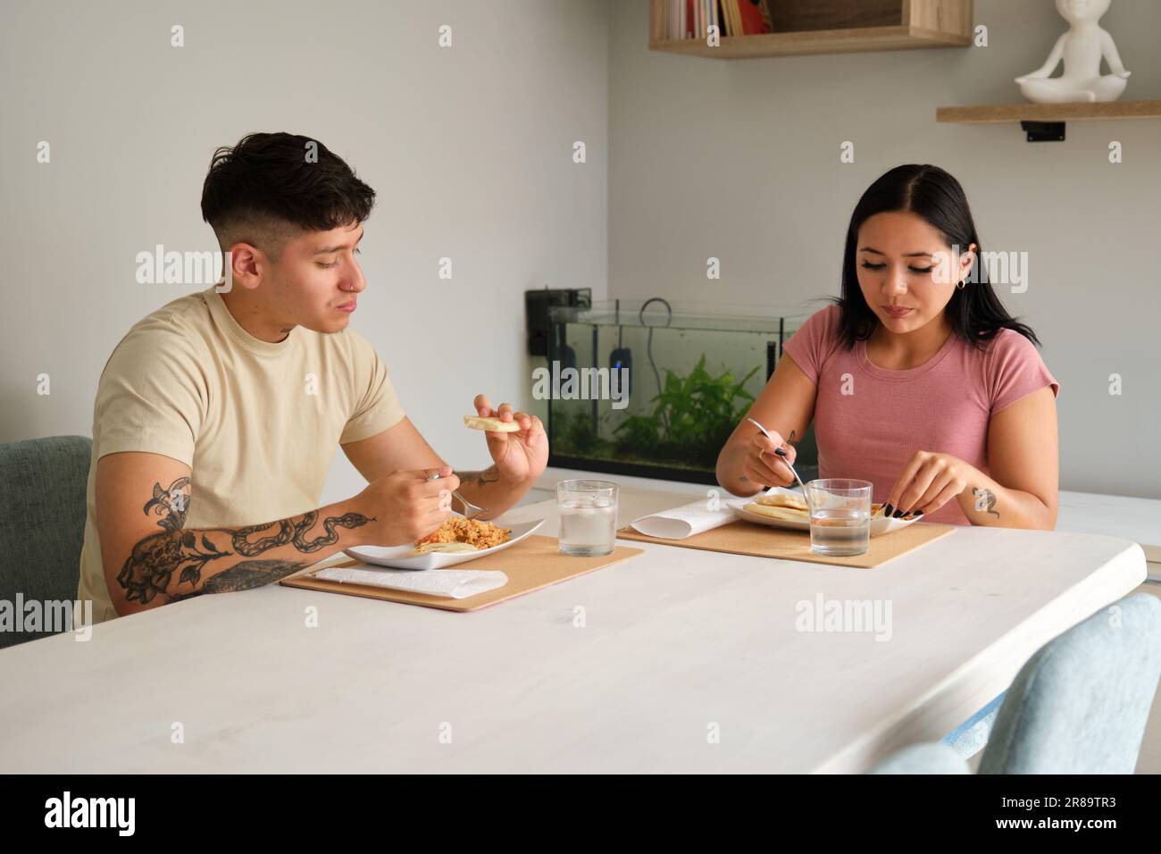 Two young hispanic people eating traditional arepas in the living room ...