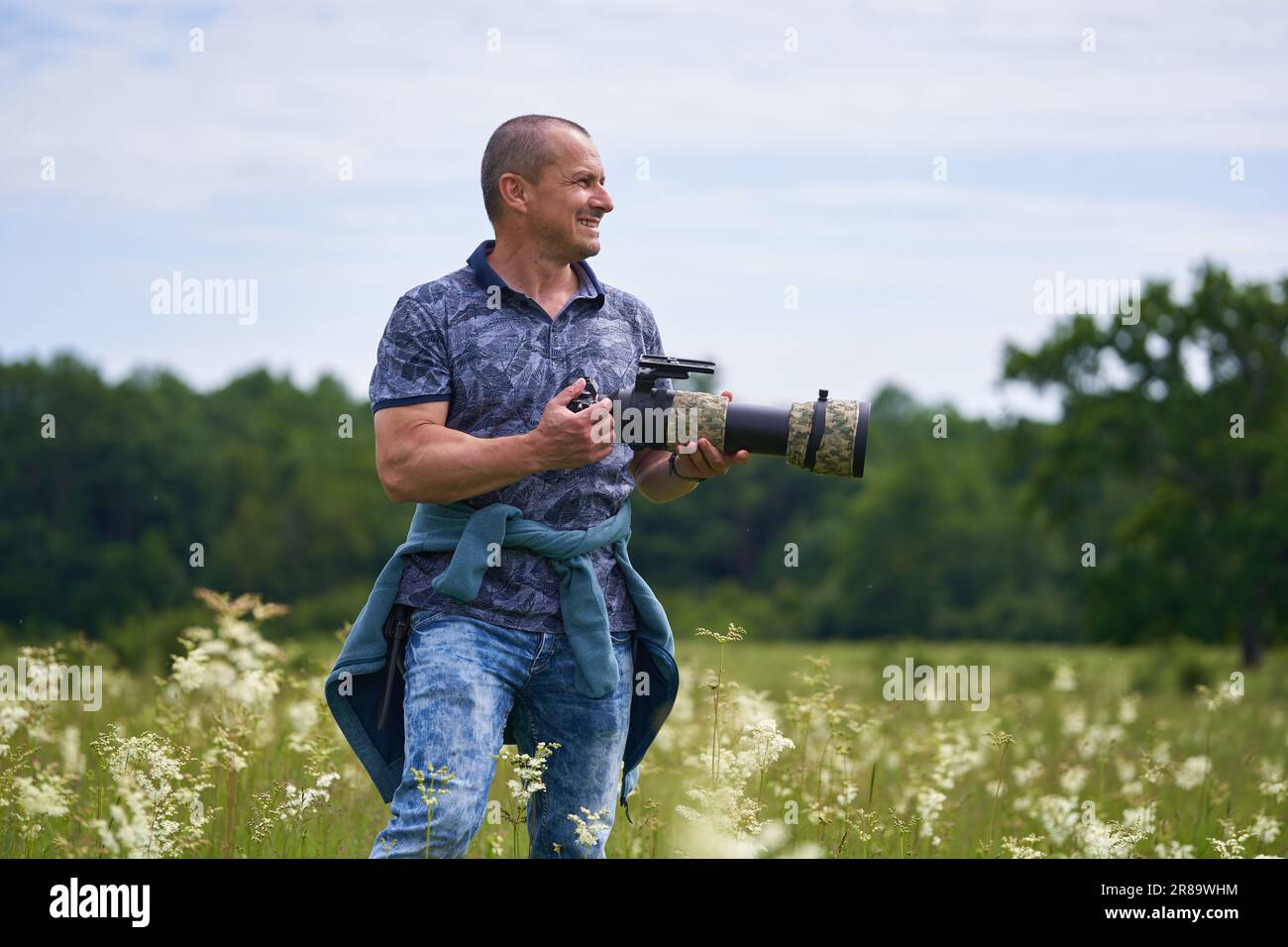 Professional nature photographer in the field by the forest, holding ...