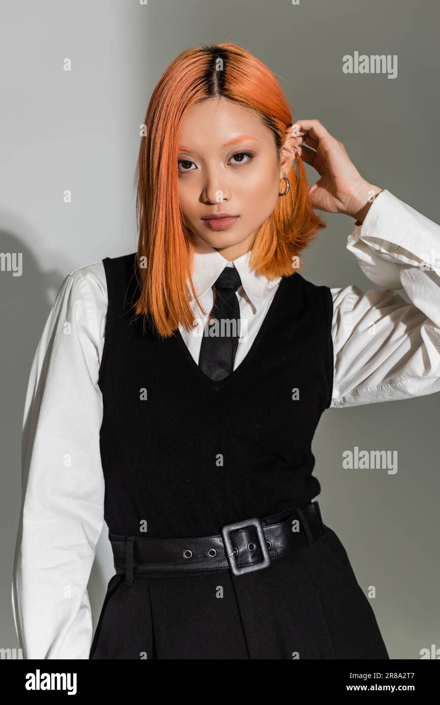 young and self-assured asian woman fixing red hair while looking at ...
