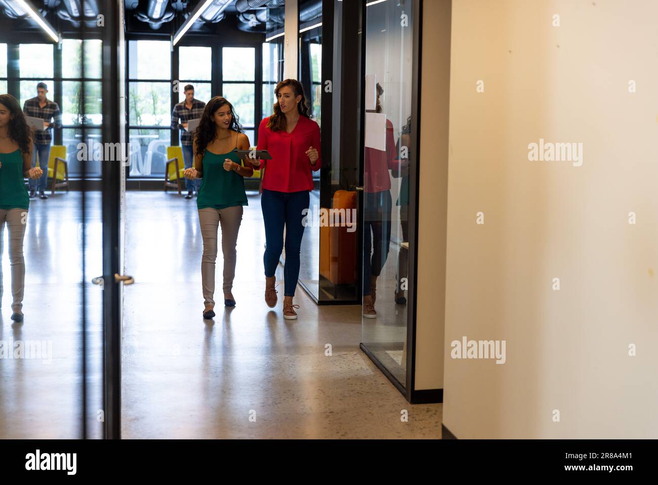 Diverse female colleagues in discussion using tablet walking in office ...