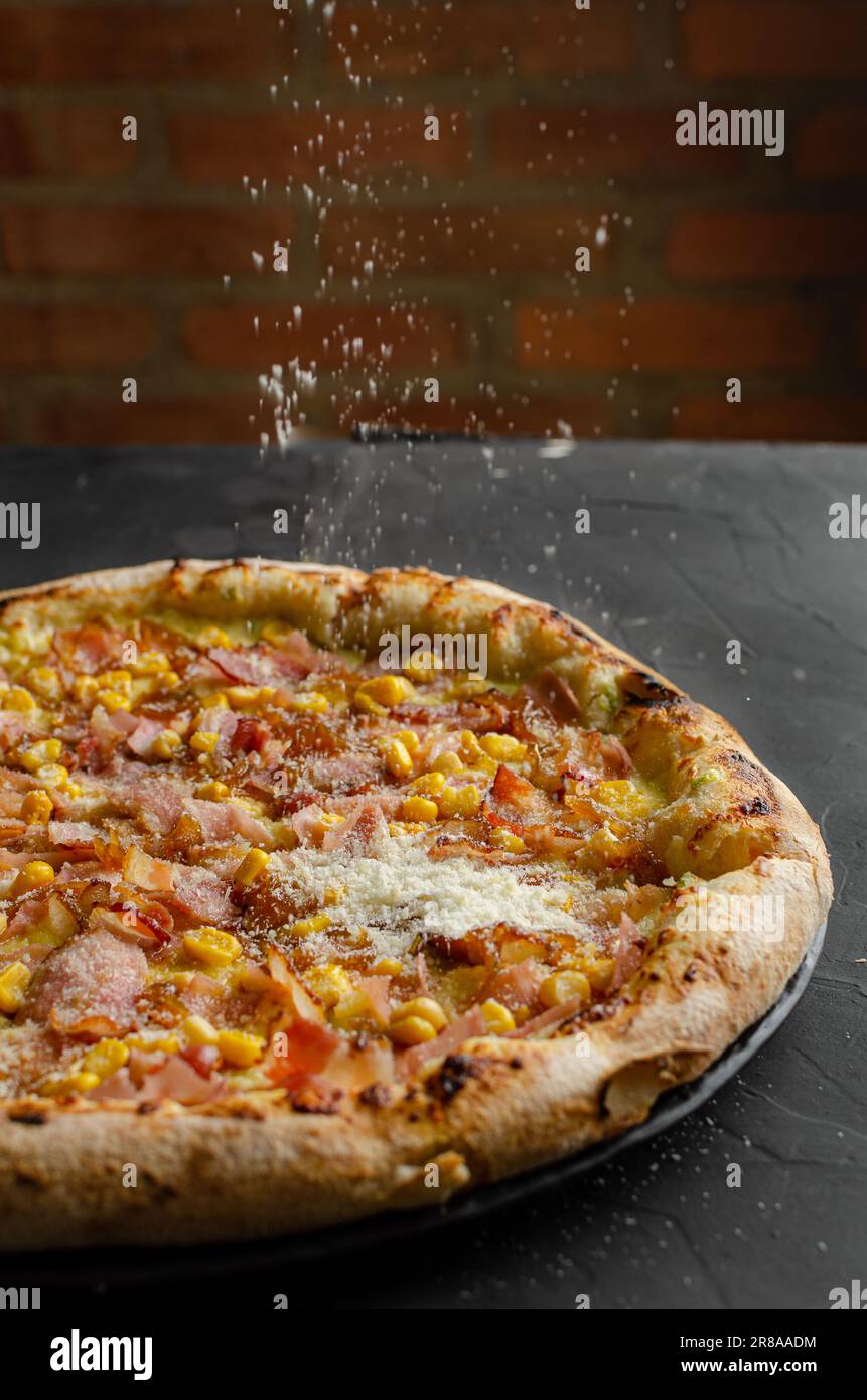 Ham and corn pizza prepared in a wood-fired oven. Black background and ...