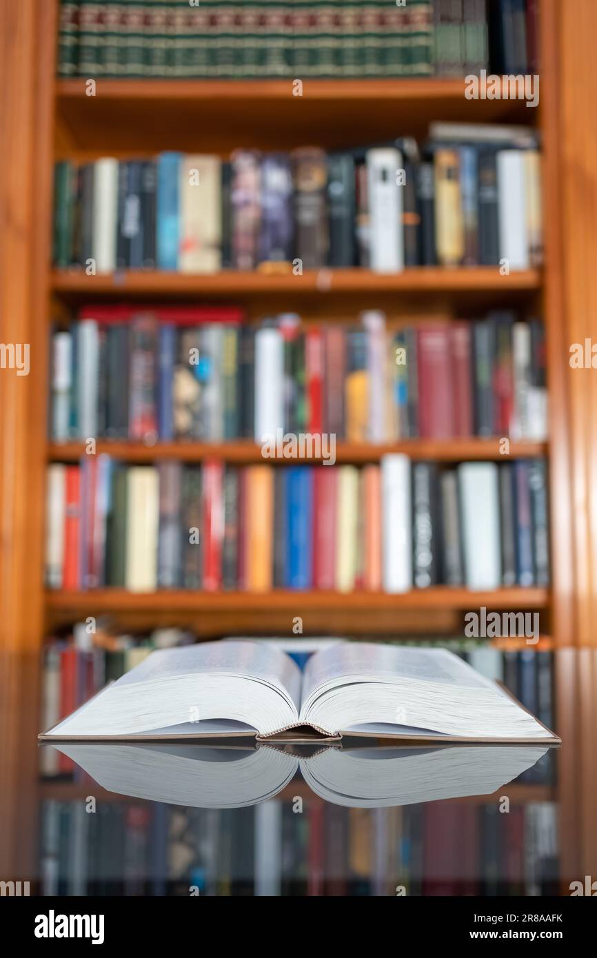 Large open book on top of a glass table with a library full of books in ...