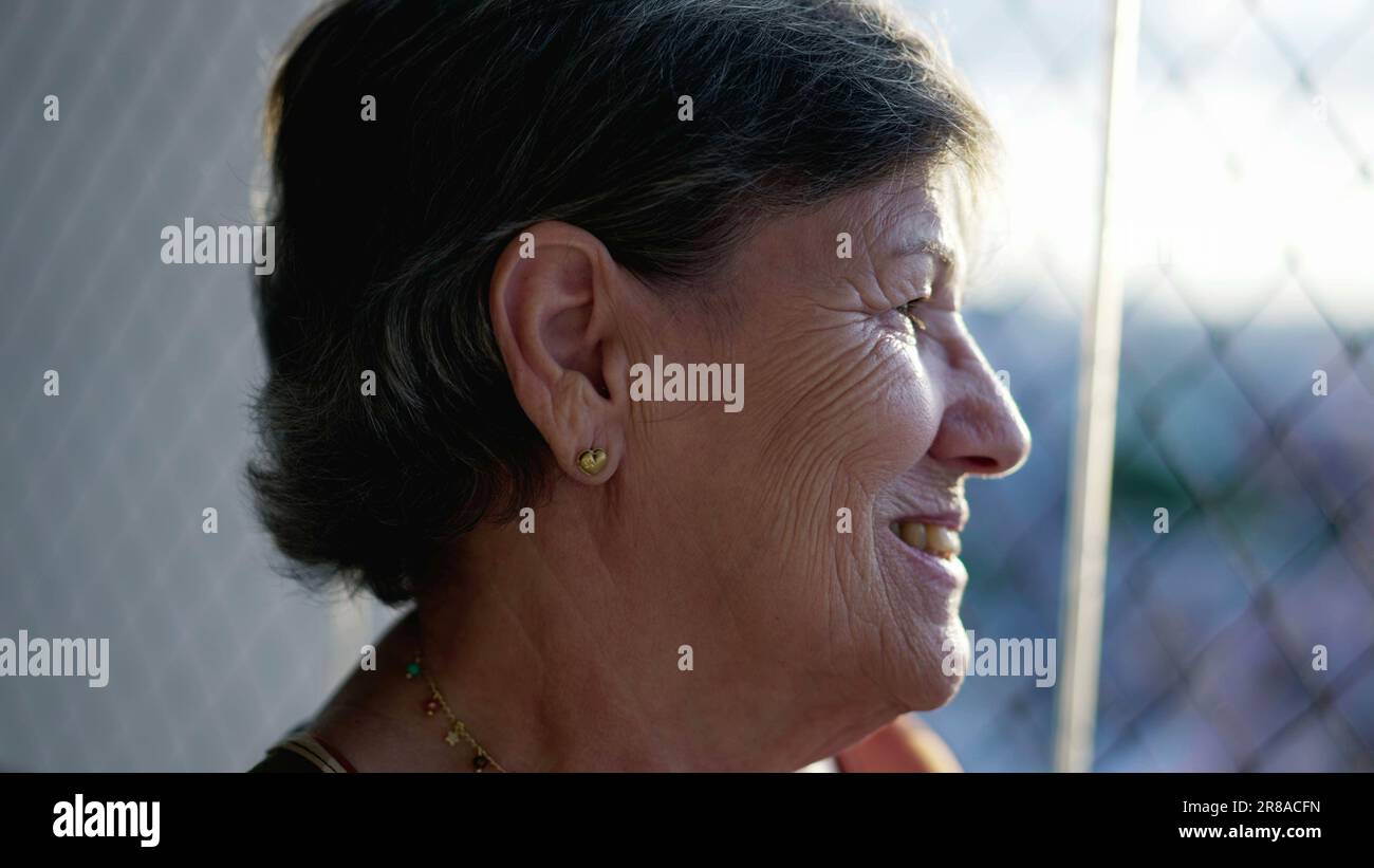 Contemplative happy older woman standing by window looking outside ...