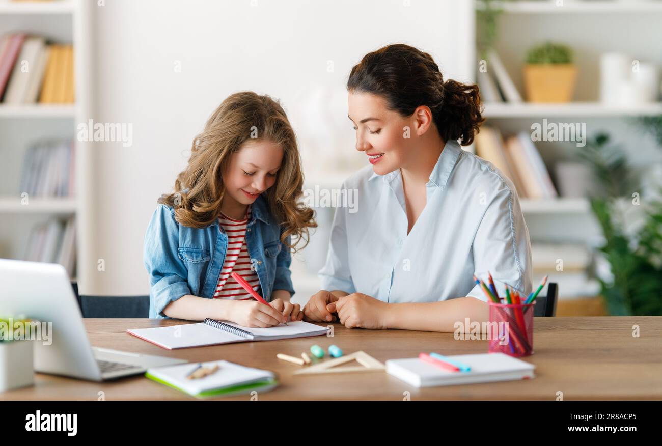 Happy child and adult are sitting at desk. Girl doing homework or ...
