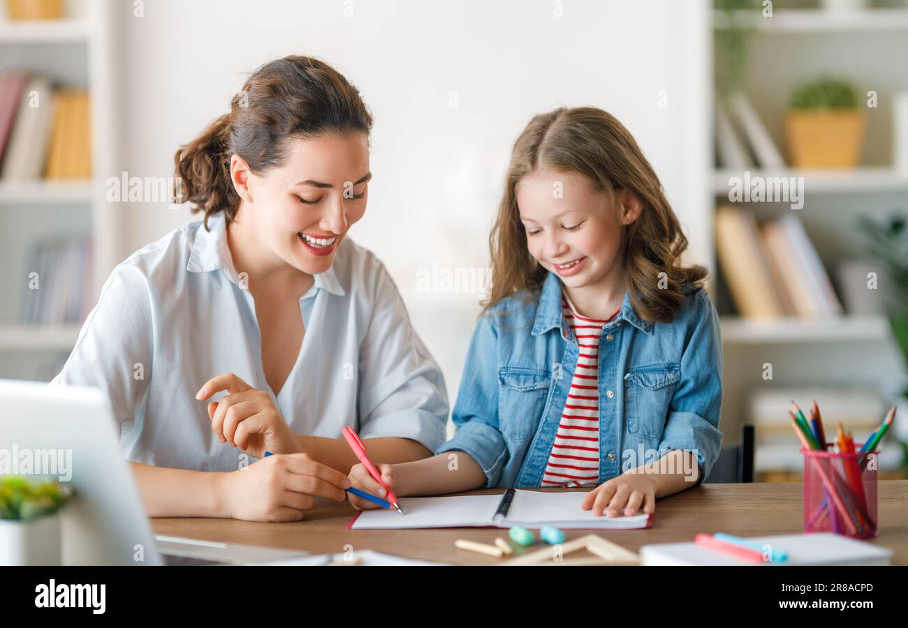 Happy child and adult are sitting at desk. Girl doing homework or ...