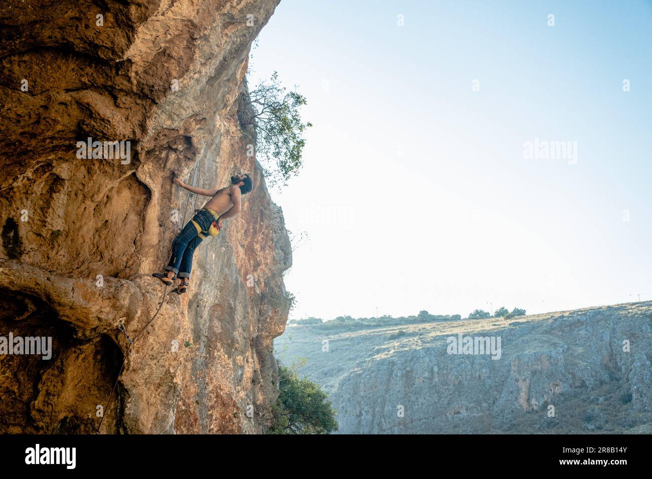 A person is scaling a cliff face, ascending the rock wall with ropes ...