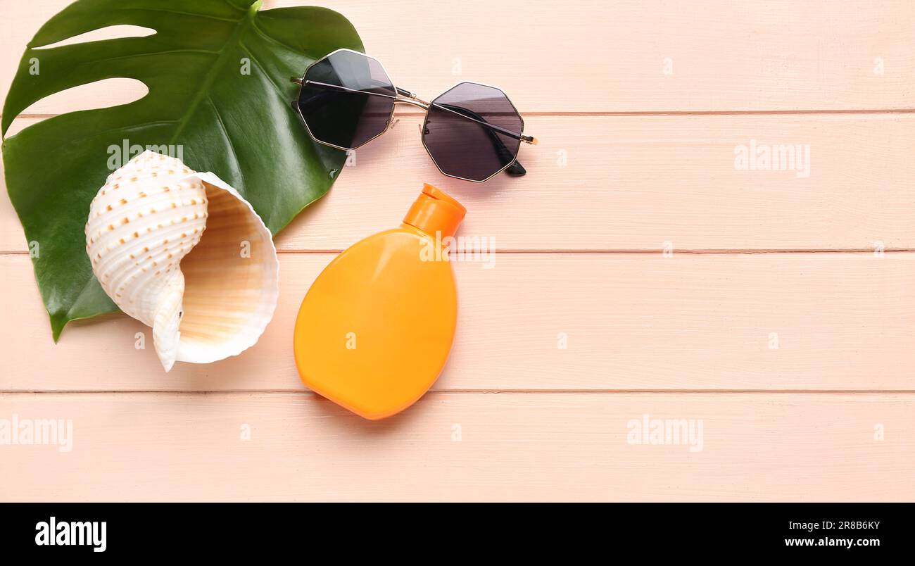 Sea shell, sunscreen cream, tropical leaf and sunglasses on wooden ...