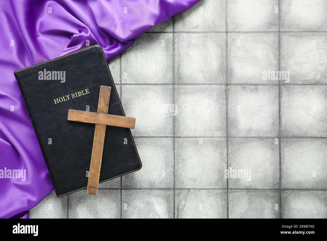 Holy Bible with wooden cross and purple fabric on grey tile background ...