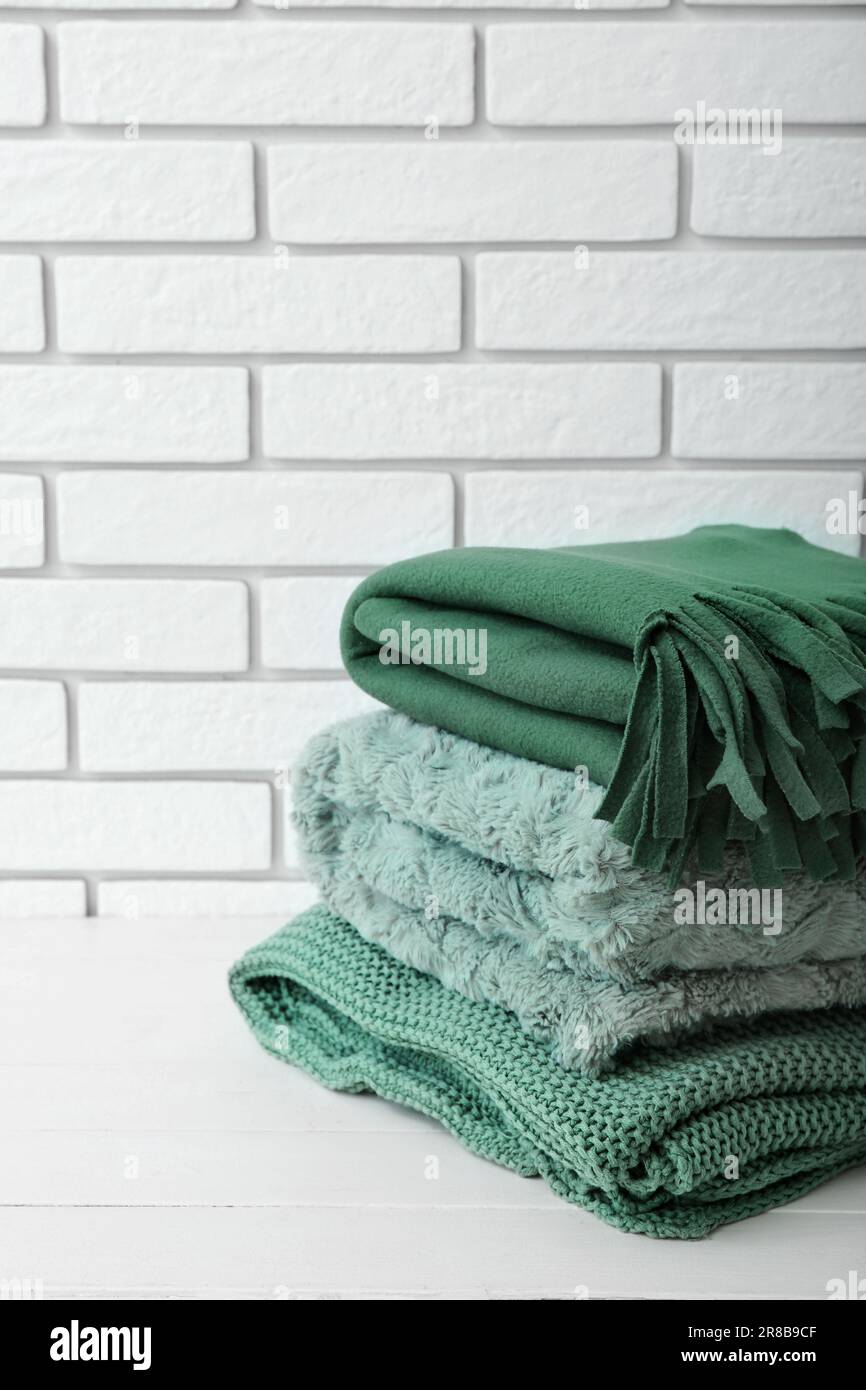 New soft folded blankets on table near light brick wall Stock Photo - Alamy