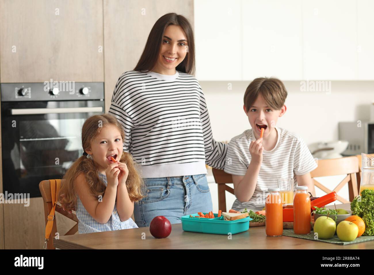 Little children with their mother eating carrots while packing school ...
