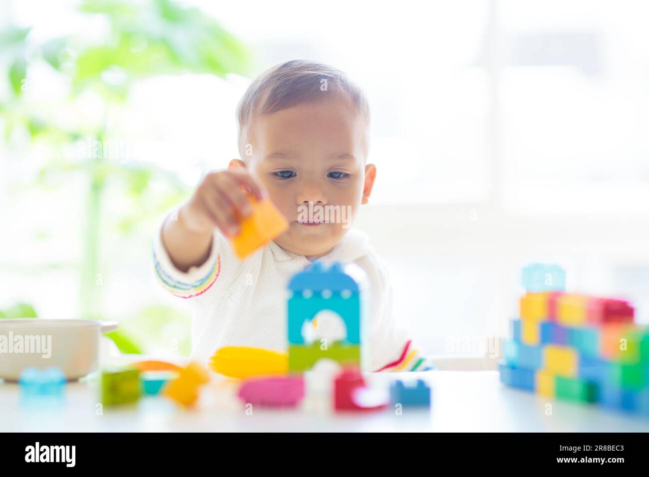 Adorable Asian baby boy playing with colorful blocks toy in white sunny ...